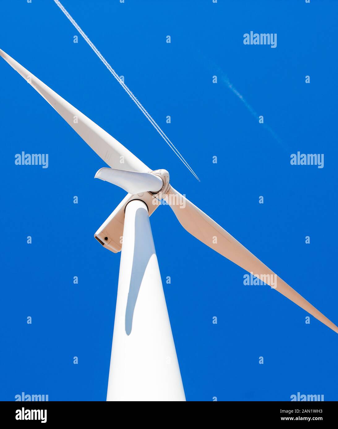 Wind turbine against a blue sky with a jet airplane passing overhead ...