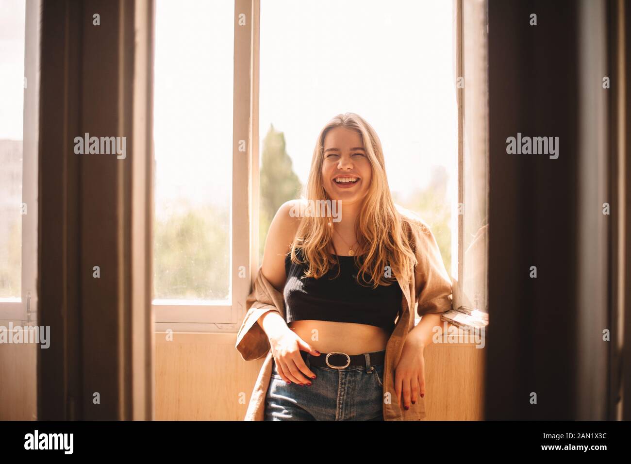 Happy young woman laughing while standing in balcony during summer ...