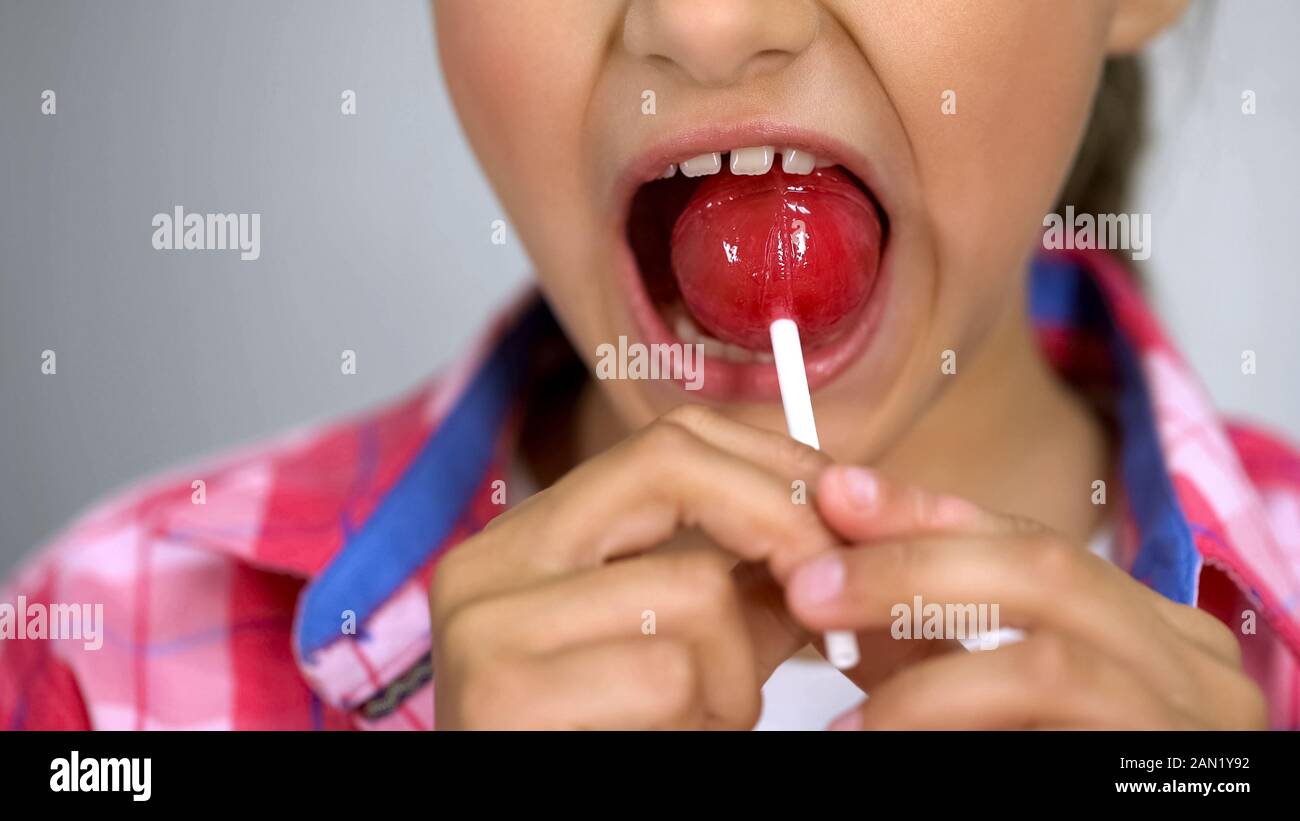 Cute little girl trying to bite lollipop, effect of sugar on teeth ...