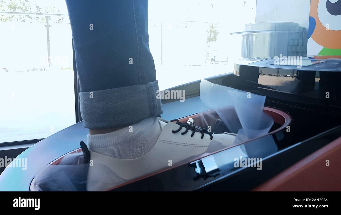 Visitor putting foot in automatic shoe cover dispenser clinic hall ...