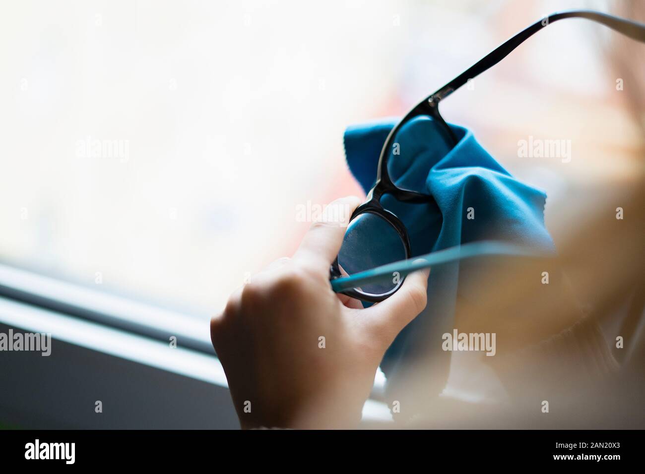 Pretty young girl cleaning her blue glasses with a blue rag. Blue ...