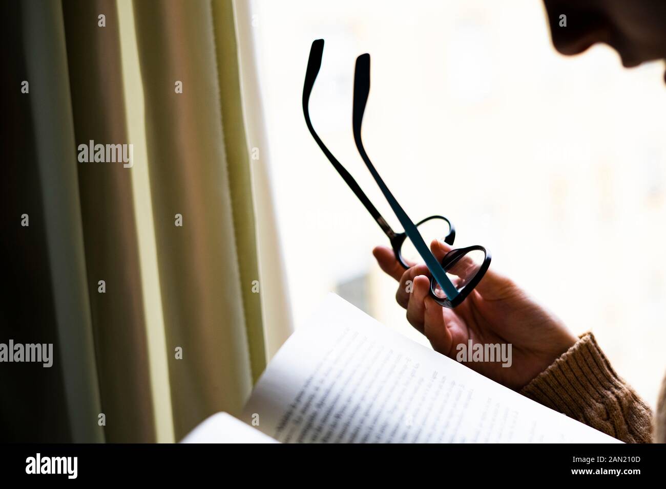 Woman reading a book with her reading glasses in her hand. Concept of ...