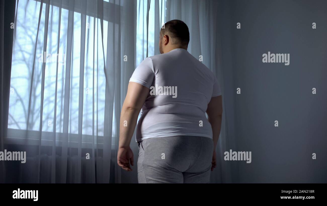 Fat man looking out through window, depressed introvert ashamed of ...