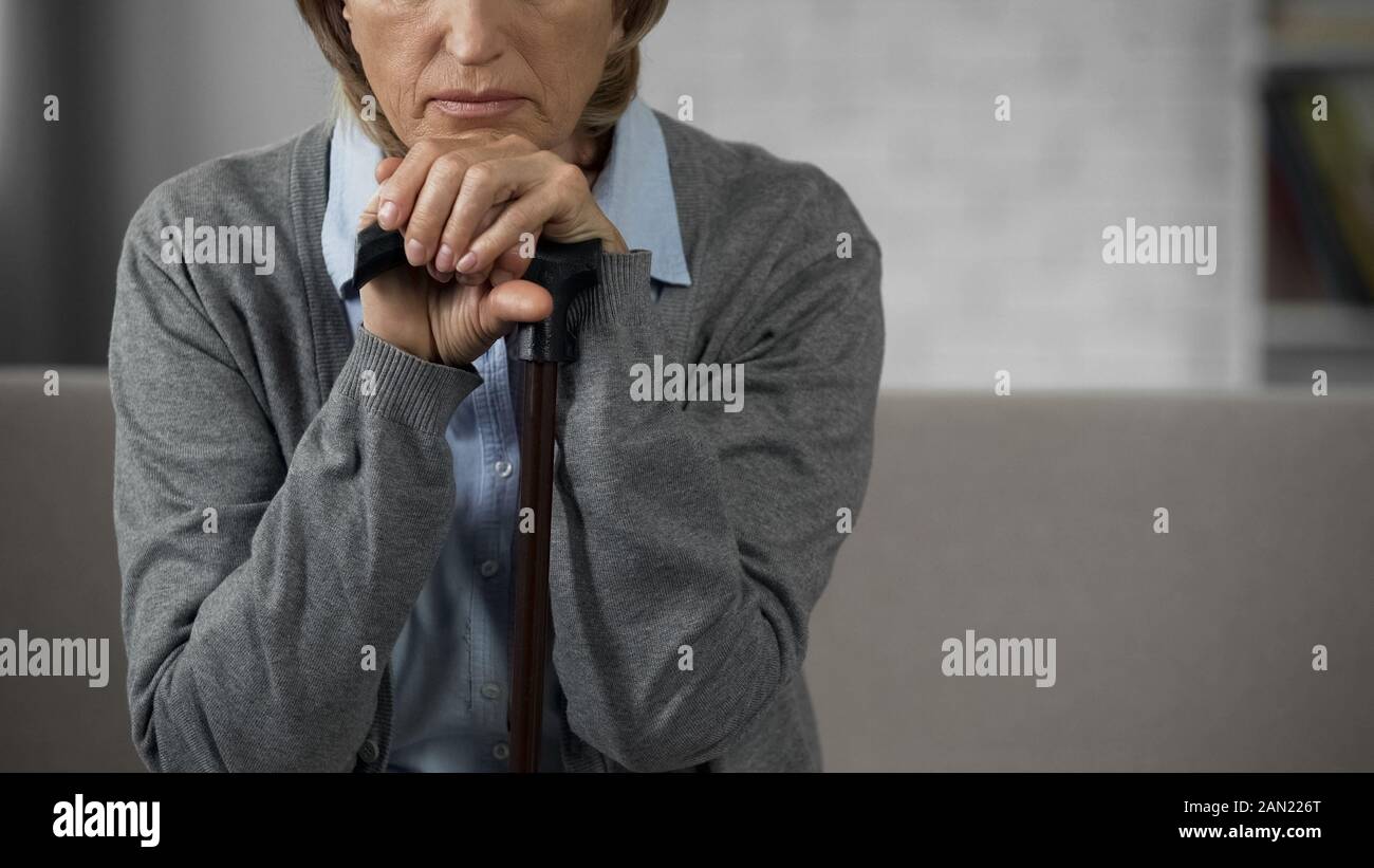 Elderly Lady Sitting Alone On Couch Holding Hands On Walking Stick