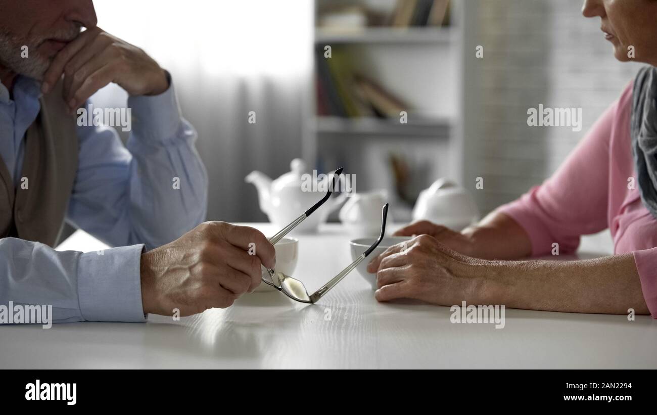 Elderly couple discussing problem sitting across table over cup of tea ...