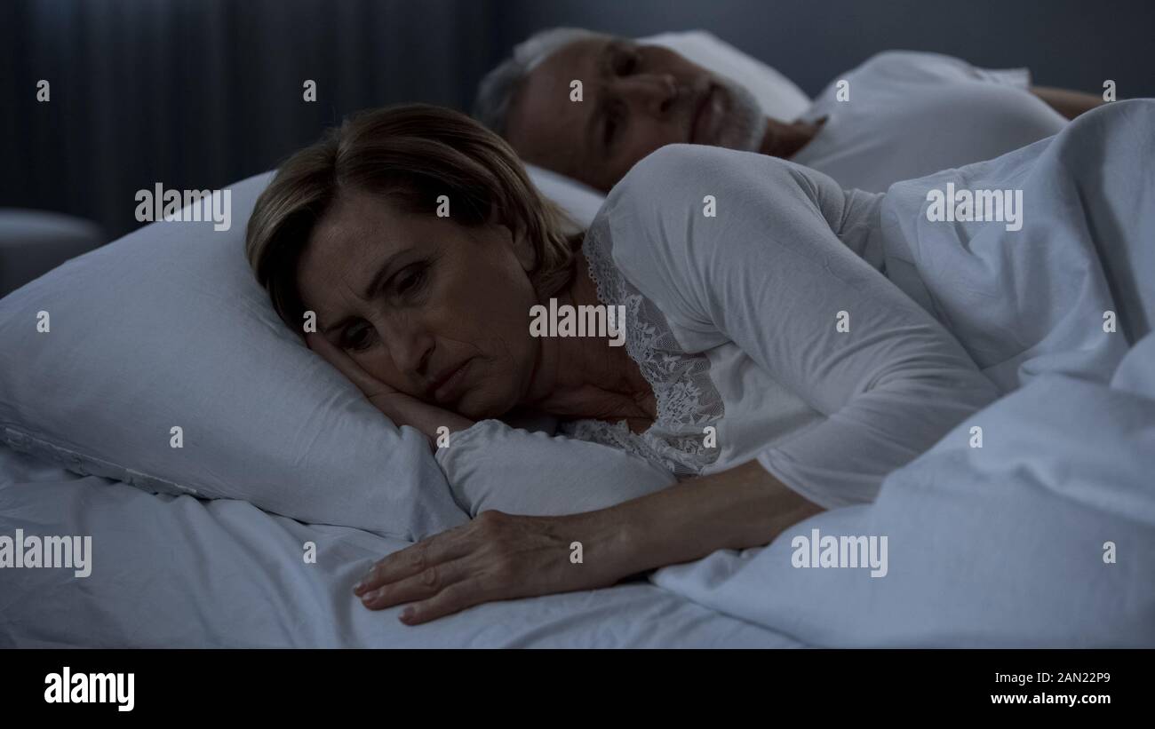 Aging couple lying sleepless in bed, woman turned back to man ...