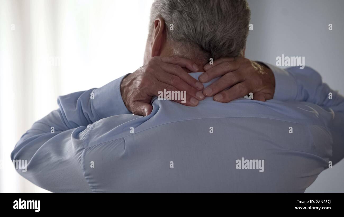 Retiree man rubbing back of his neck, standing backwards, office desk ...