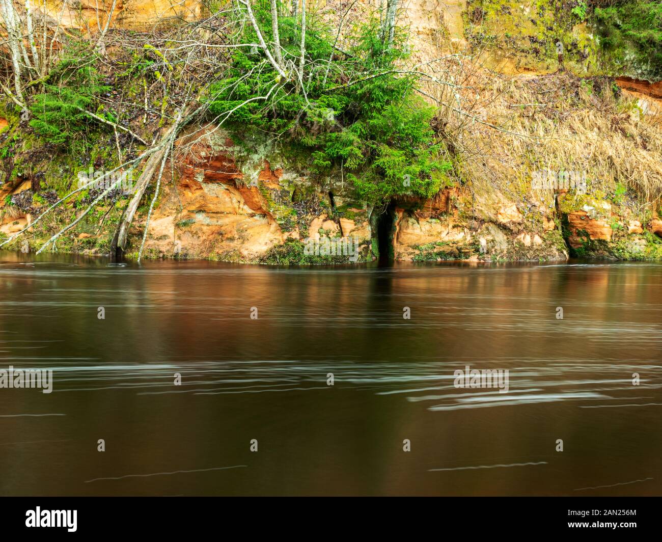 a landscape with a steep river and caves on a sandstone cliff, a cloudy ...
