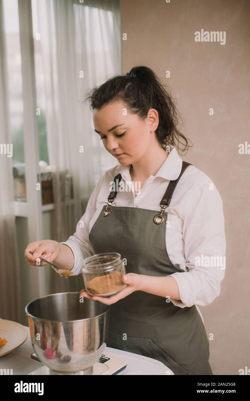 The cook girl pours brown cane sugar into a metal bowl. Cooking sweets ...