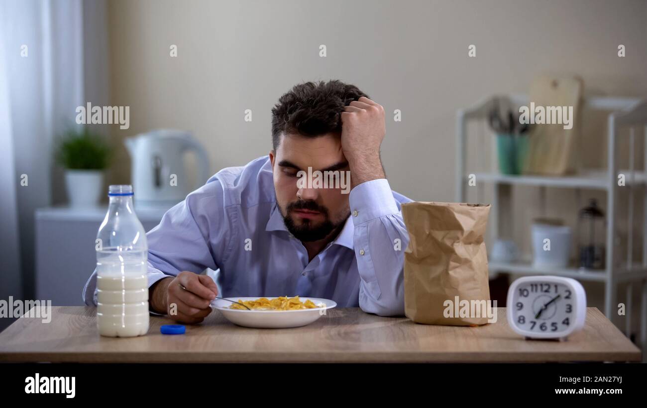 Extremely tired young bachelor sleeping over plate with corn flakes ...
