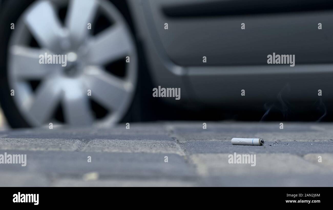Driver throwing stub of cigarette from car window on pavement, dirty ...