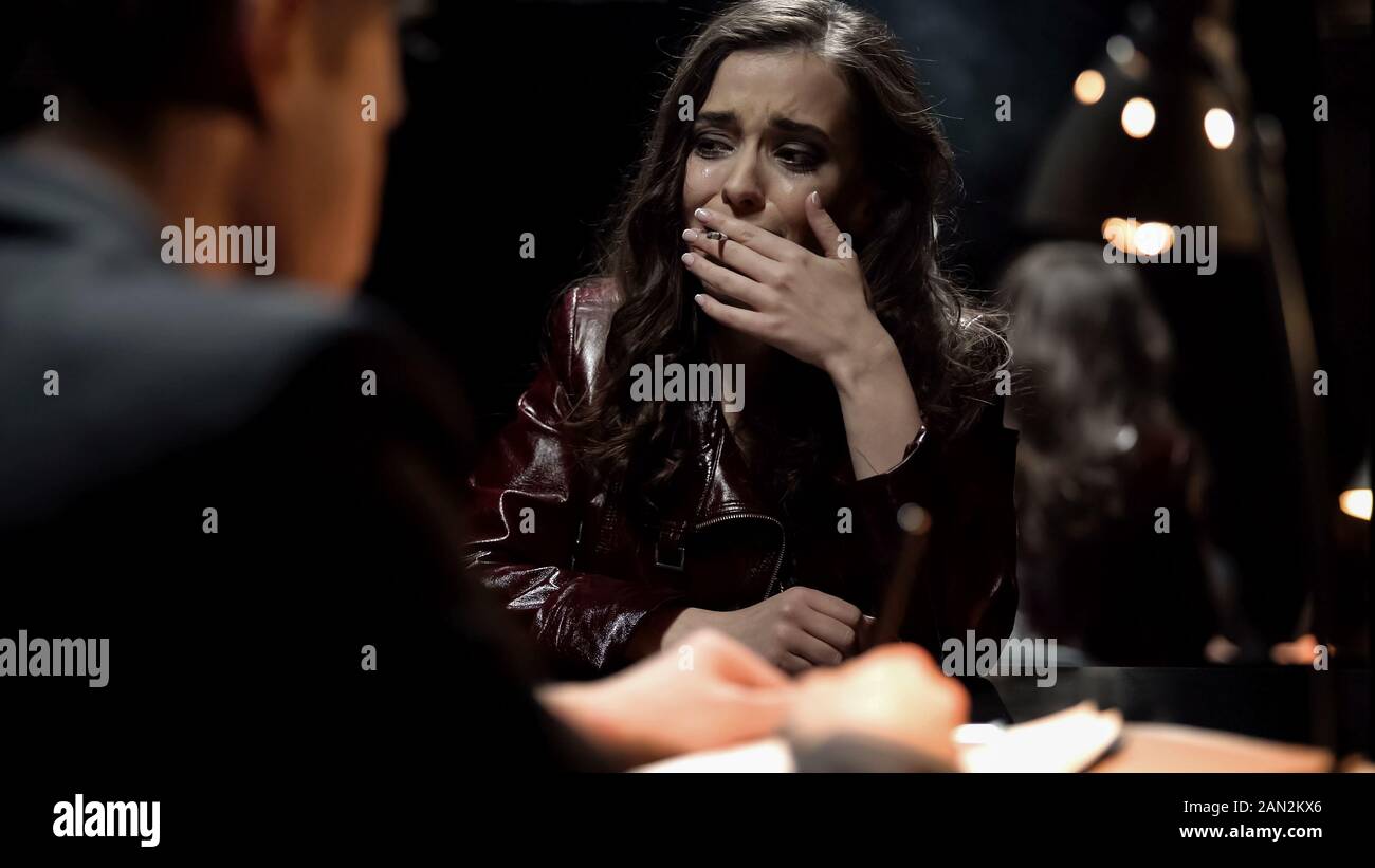 Crying woman smoking cigarette in interrogation room, giving evidence ...