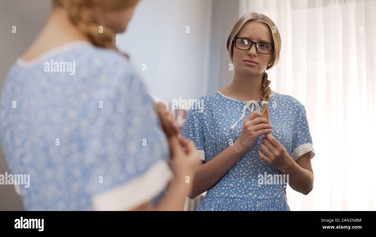 Female geek in glasses looking in the mirror, feeling bad of poor ...