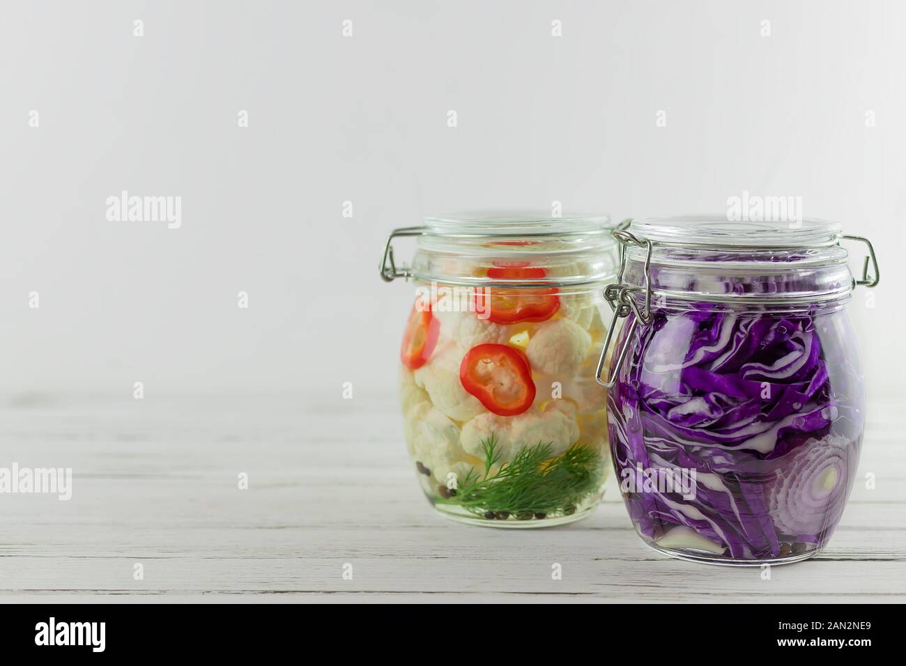 two glass jars of fermented red cabbage, cauliflower. vegetables on a ...