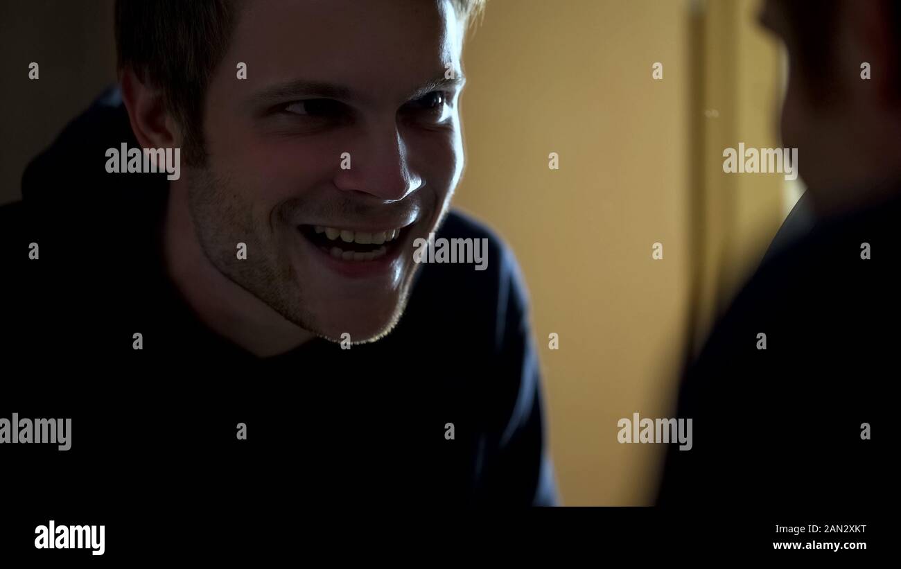 Nervous criminal smiling into mirror after crime, mentally unbalanced ...