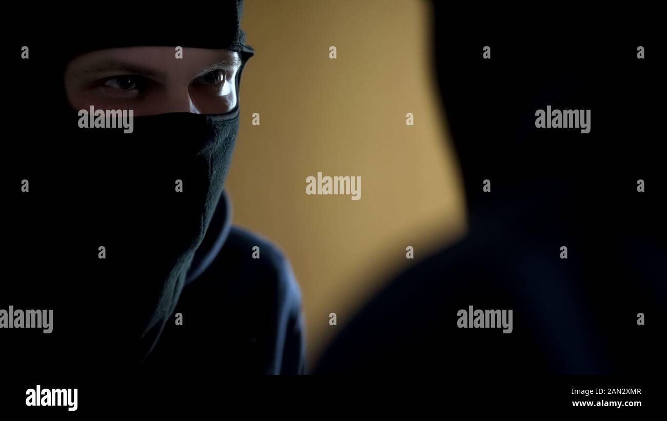 Crazy maniac wearing black face mask, looking at reflection in mirror ...