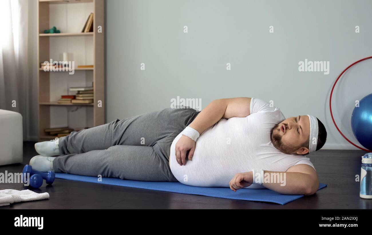 Overweight man breathing heavily after exercises on mat, desire to lose ...