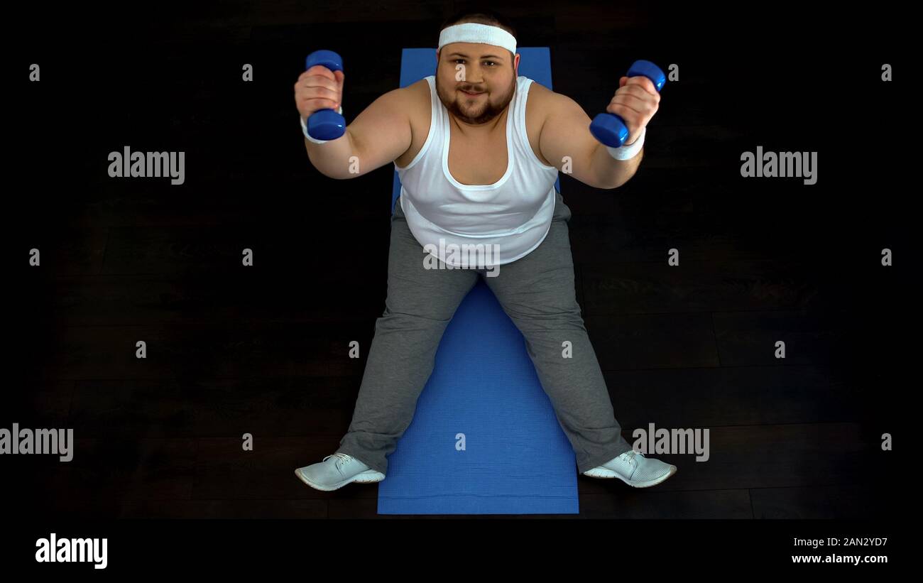 Active fat man lifting dumbbells sitting on mat, sport motivation ...