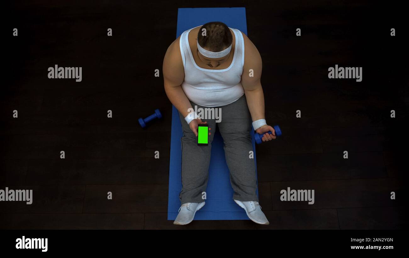 Lazy fat man lifting dumbbell and watching video on smartphone, burning ...