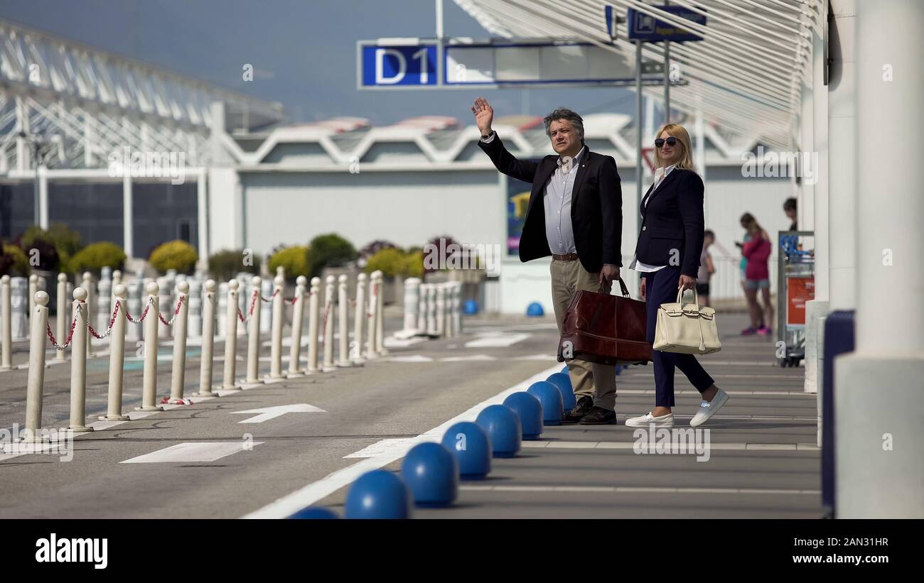 Middle-aged male and female leaving airport and hailing taxi, traveling ...