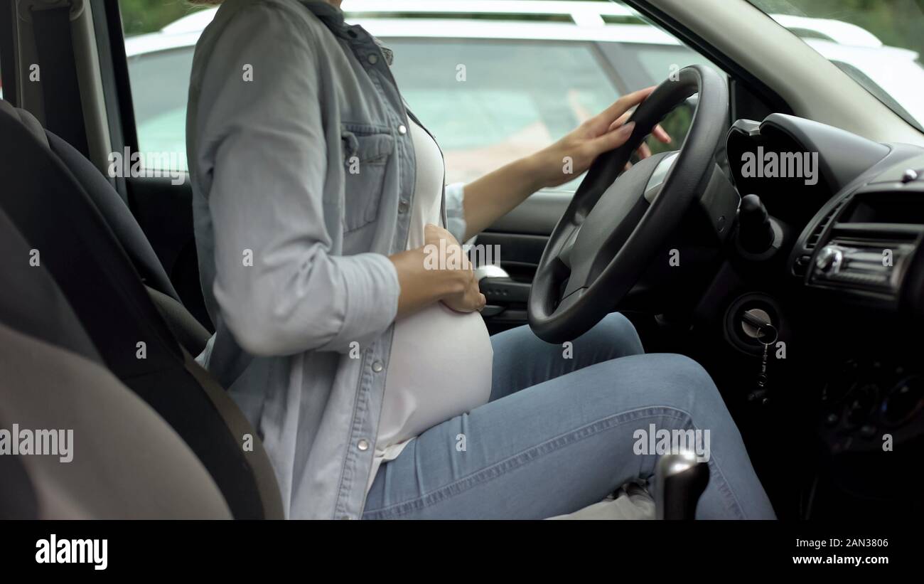 Pregnant woman in car, holding hand on belly, active baby during third ...