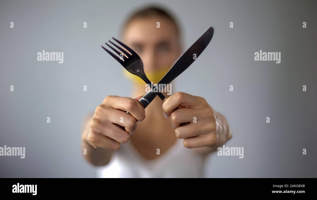 Woman crossing fork and knife, mouth closed with tape, self-restriction ...