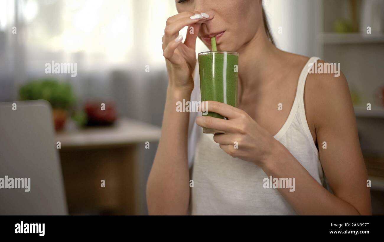 Woman drinking disgusting green smoothie, closing nose, bad smell and ...