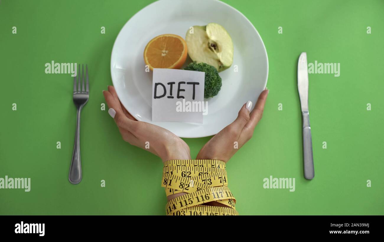 Diet note on plate with fruits and vegetables, hands tied with ...