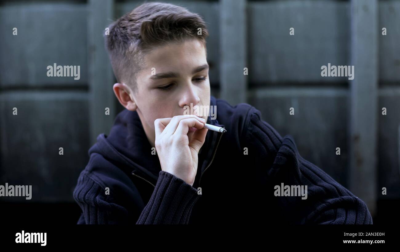 Teenager boy smoking cigarette in gateway, hiding from parents, bad ...