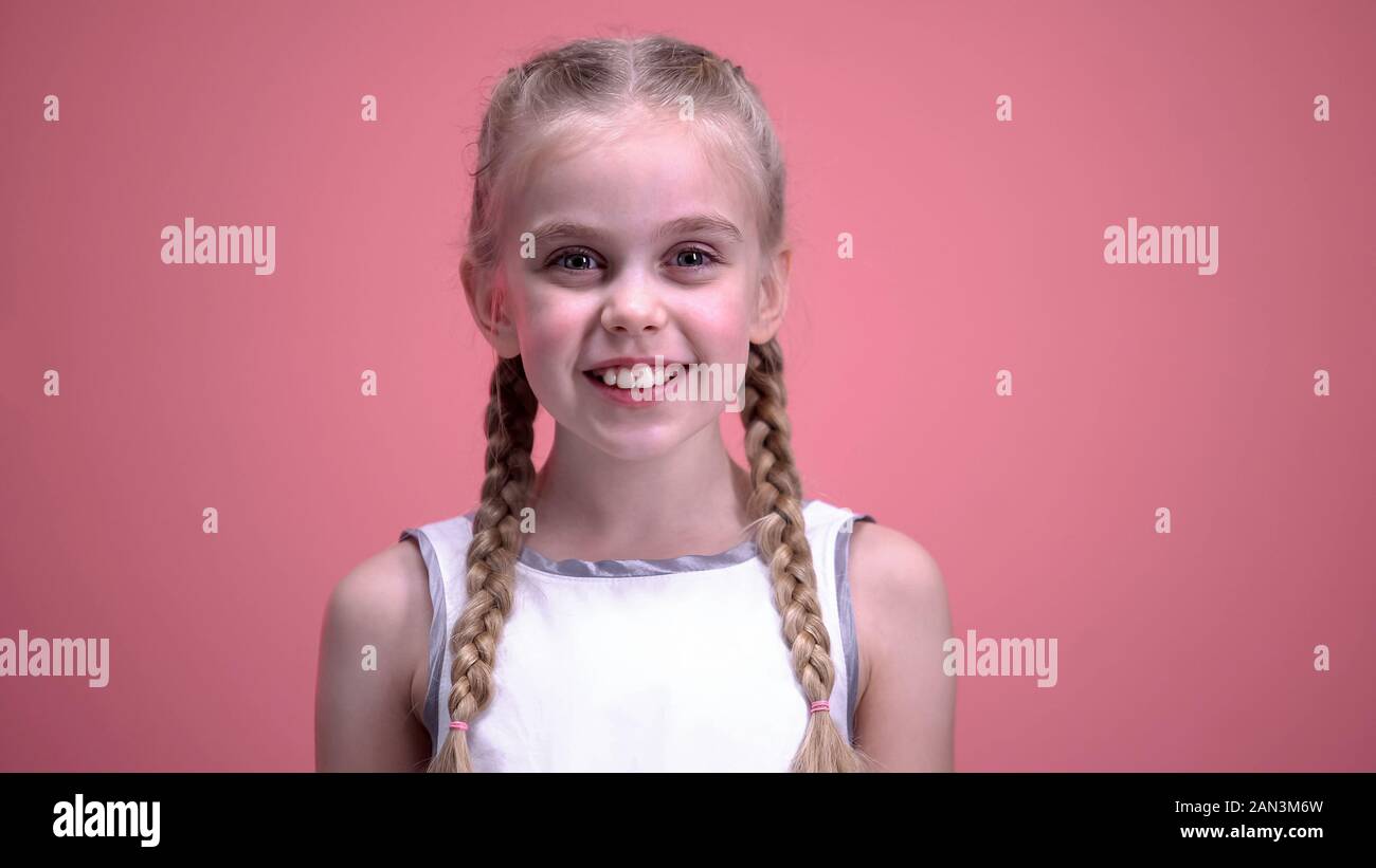 Pretty female kid with braids smiling on camera against pink background ...
