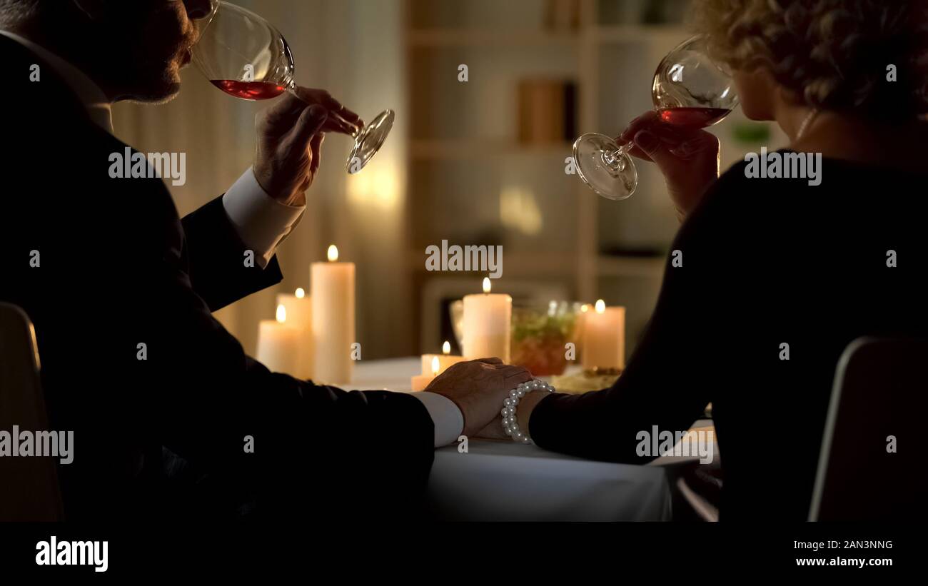 Elegant married couple drinking wine and holding hands, tender ...