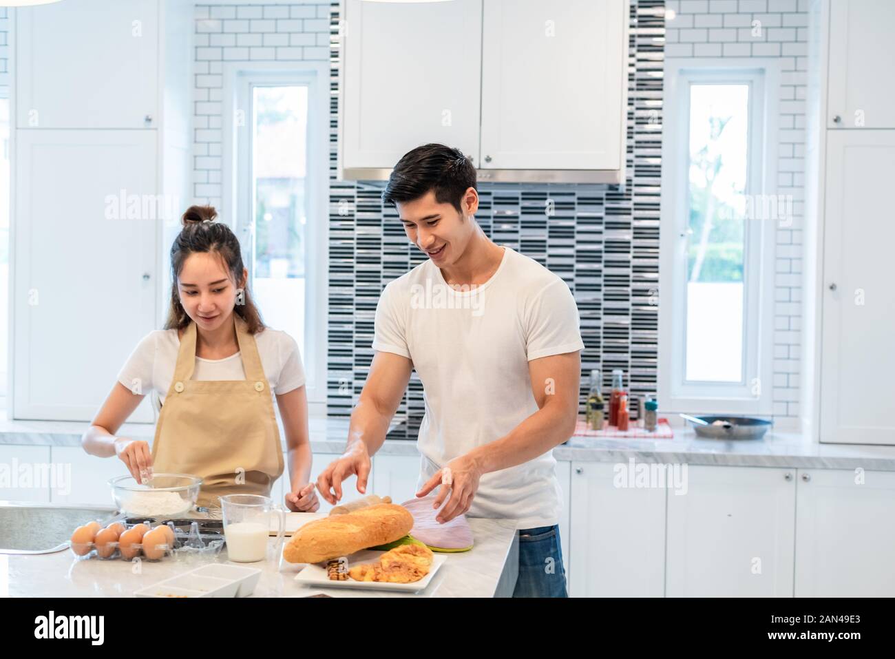 Happy Asian couples cooking and baking cake together in kitchen room ...