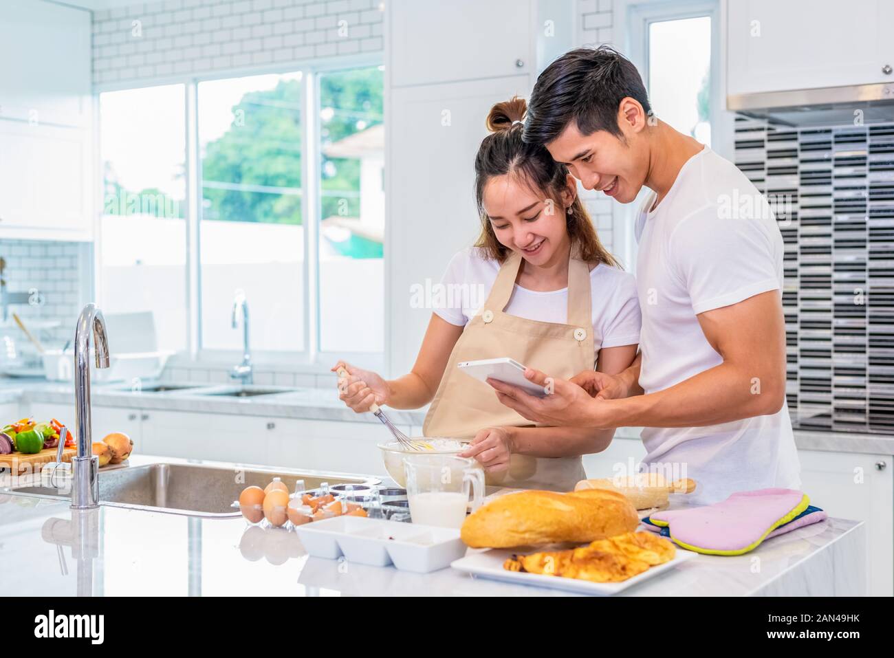 Happy Asian couples cooking and baking cake together in kitchen room ...