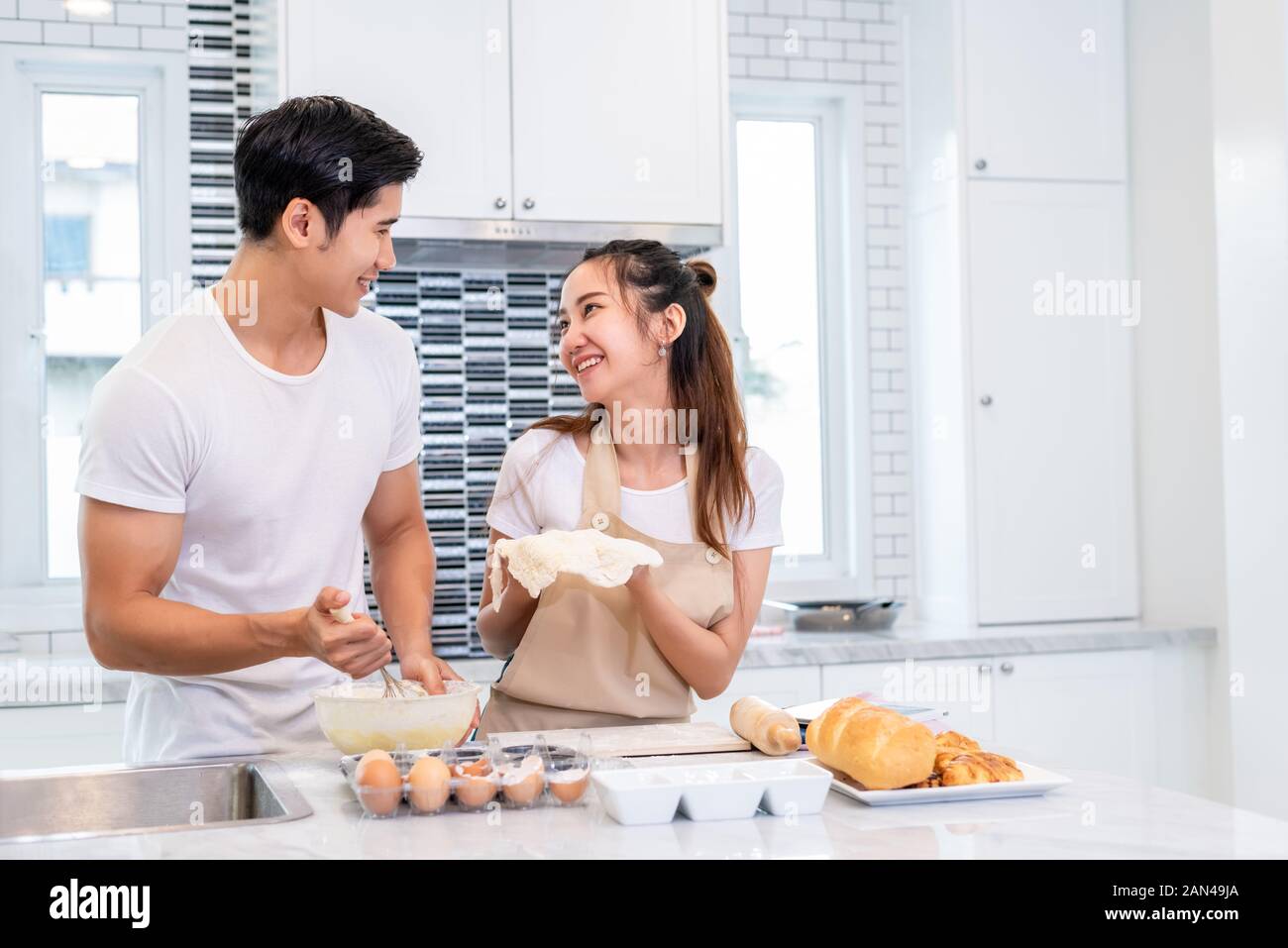 Happy Asian couples cooking and baking cake together in kitchen room ...