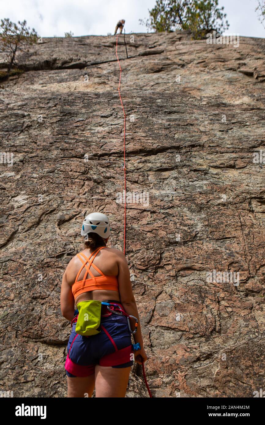 An advanced rock climber is seen at the summit of a steep cliff, fixing ...