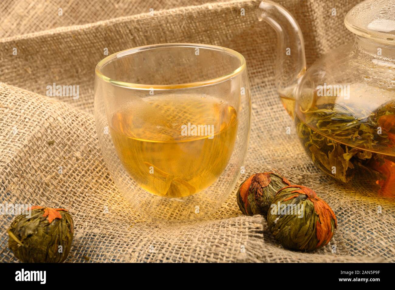 Flower tea brewed in a glass teapot, a glass of flower tea and balls of ...