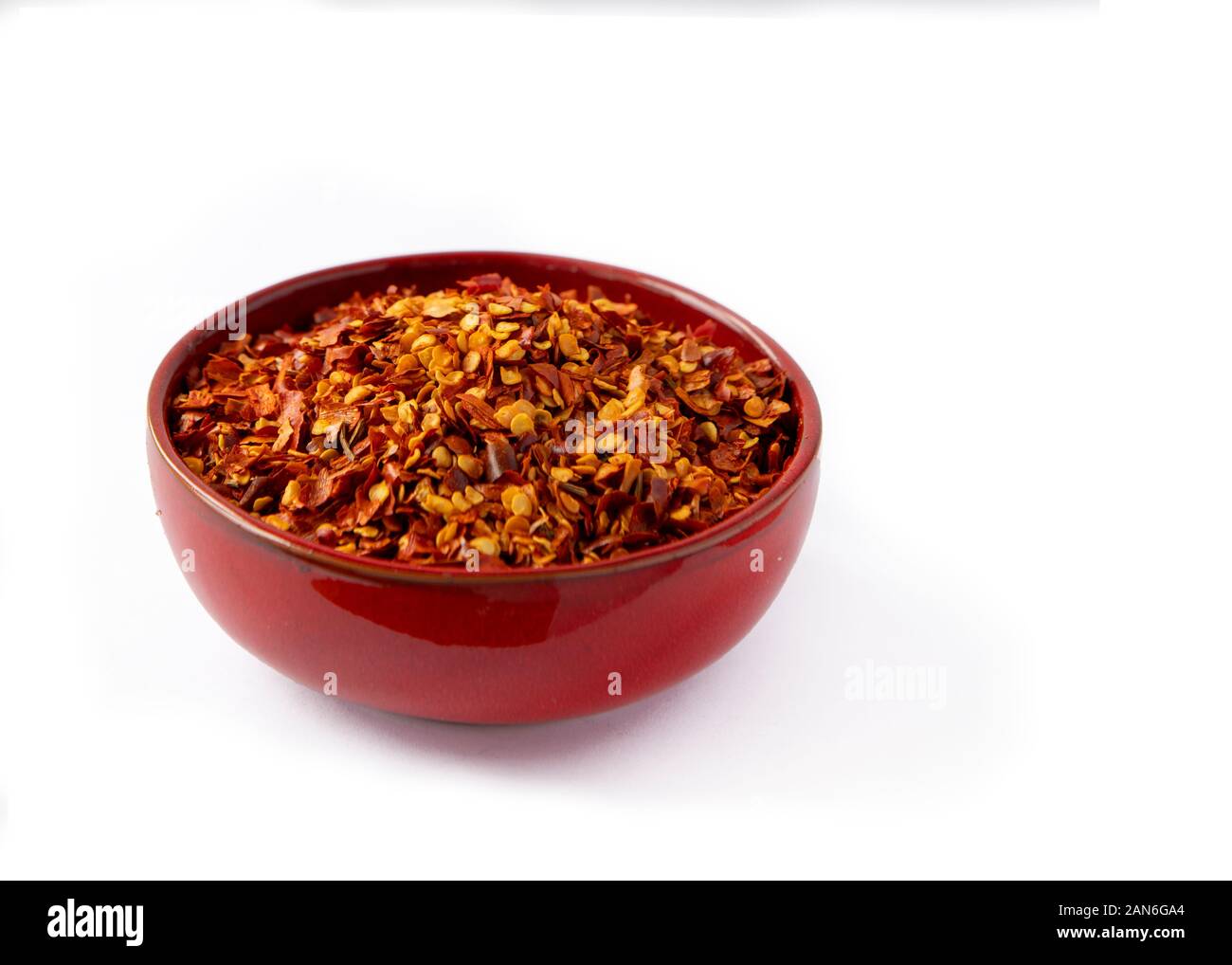 Hot chilli flakes and seeds in a red colored bowl isolated on a white ...