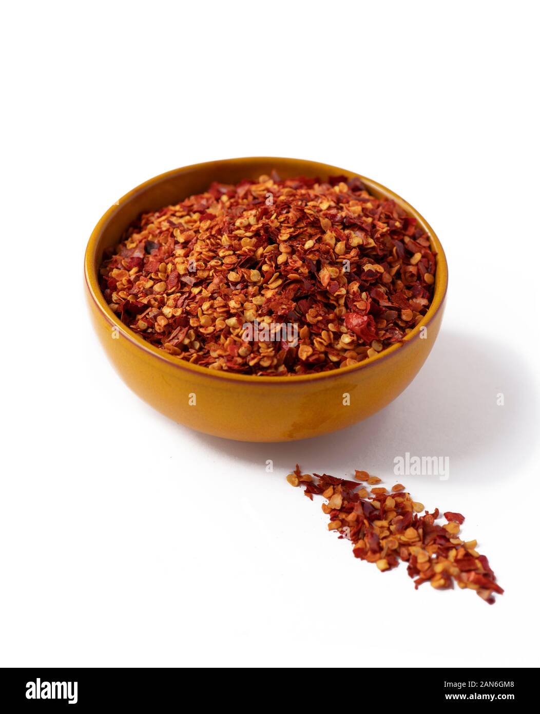 Hot chilli flakes in a mustard colored bowl isolated on a white ...