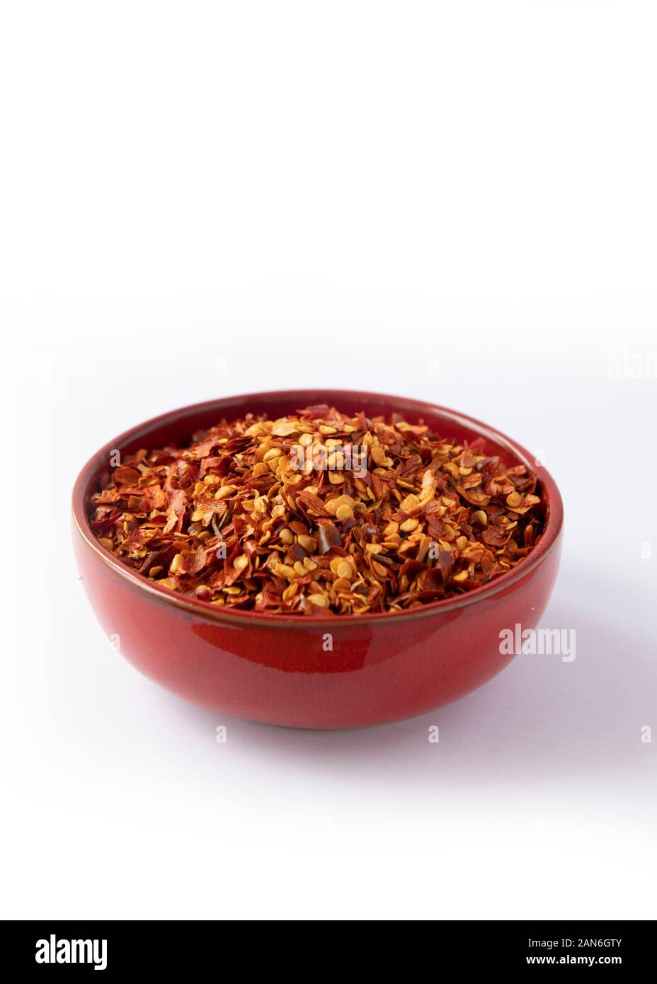 Organic chilli flakes in a red colored bowl isolated on a white ...