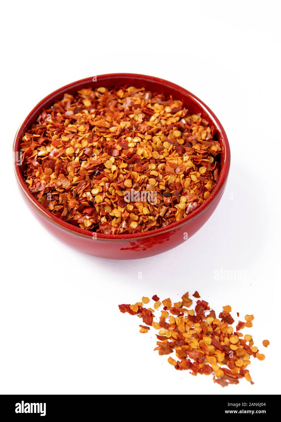 Hot chilli flakes in a red colored bowl vertical isolated on a white ...