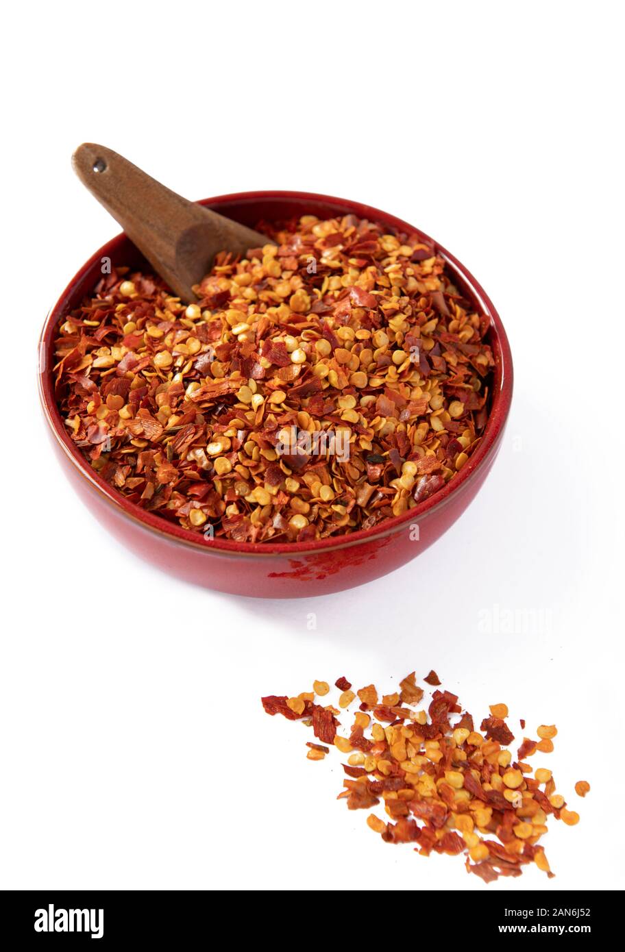 vertical , chilli flakes in a red colored bowl with small wooden spoon ...