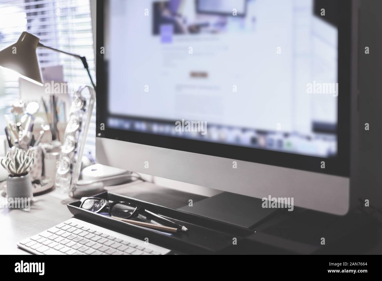 Blurred large computer screen on a home office desk interior eith work ...