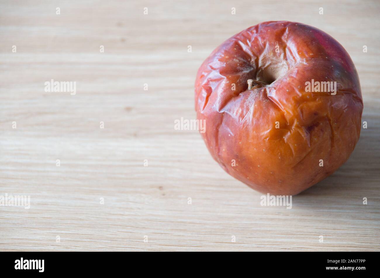 Old rotten apple isolated on a wooden bench top covered in wrinkles and ...