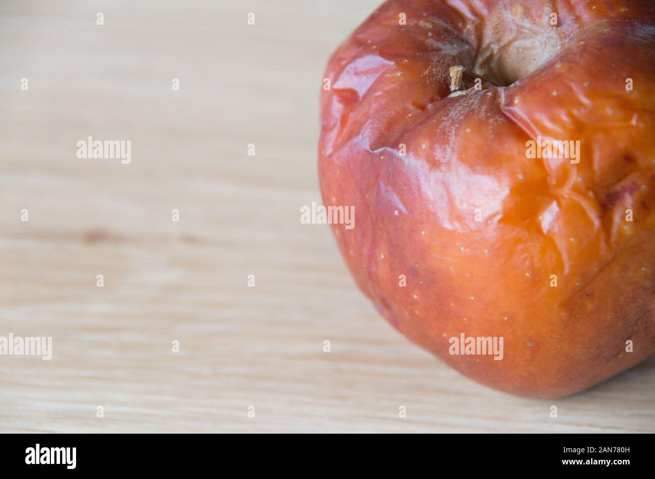 Old rotten apple isolated on a wooden bench top covered in wrinkles and ...