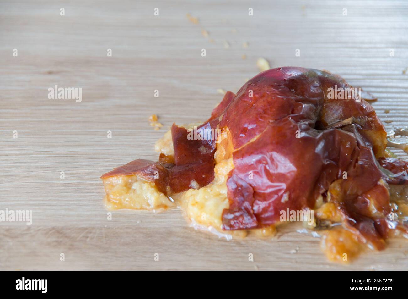 Old squashed rotten apple isolated on a wooden bench top covered in ...