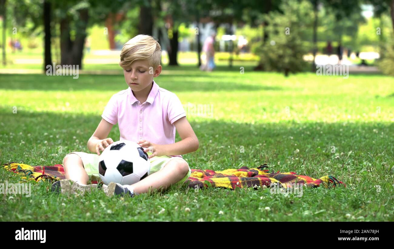 Sad boy sitting lonely in park, playing with football alone, bullying ...