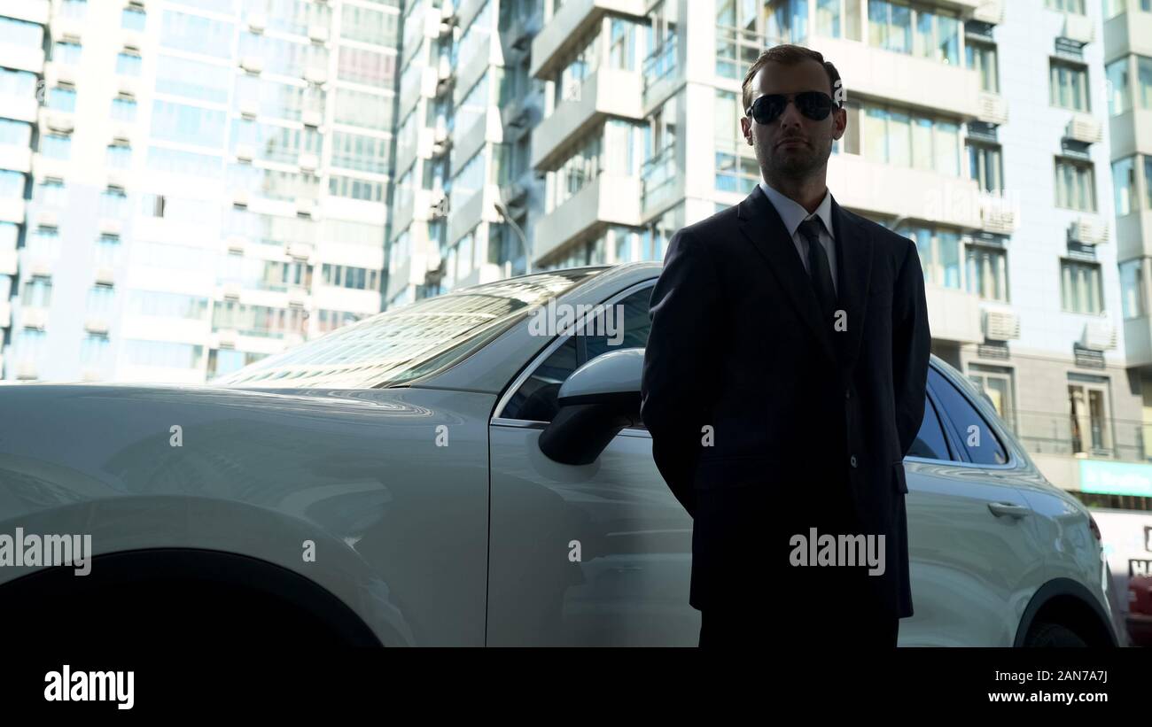 Masculine bodyguard standing near vehicle, providing security for vip ...