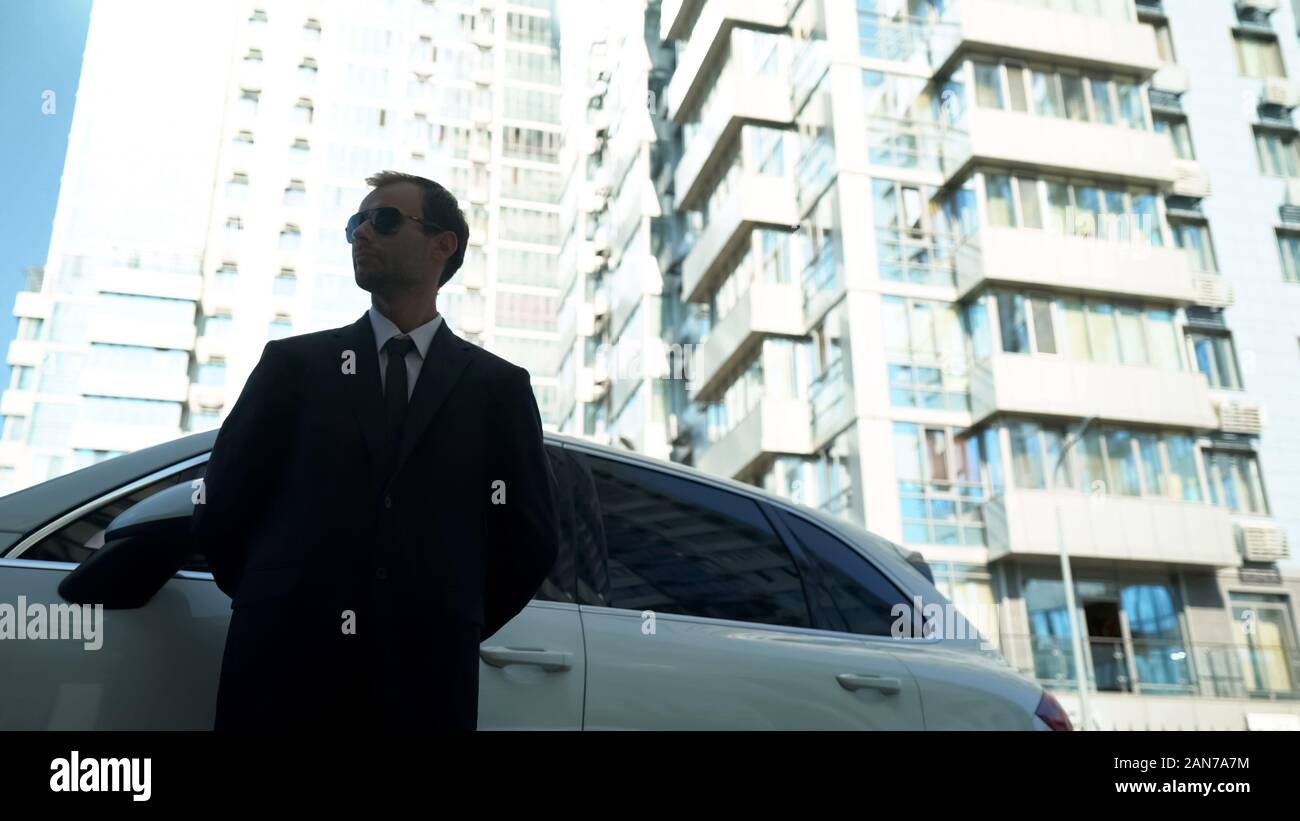 Bodyguard standing near business car, checking safety and security ...