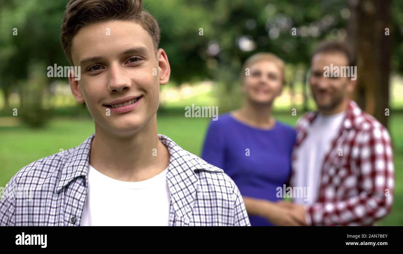 Teenage boy smiling on background of cheerful hugging parents ...