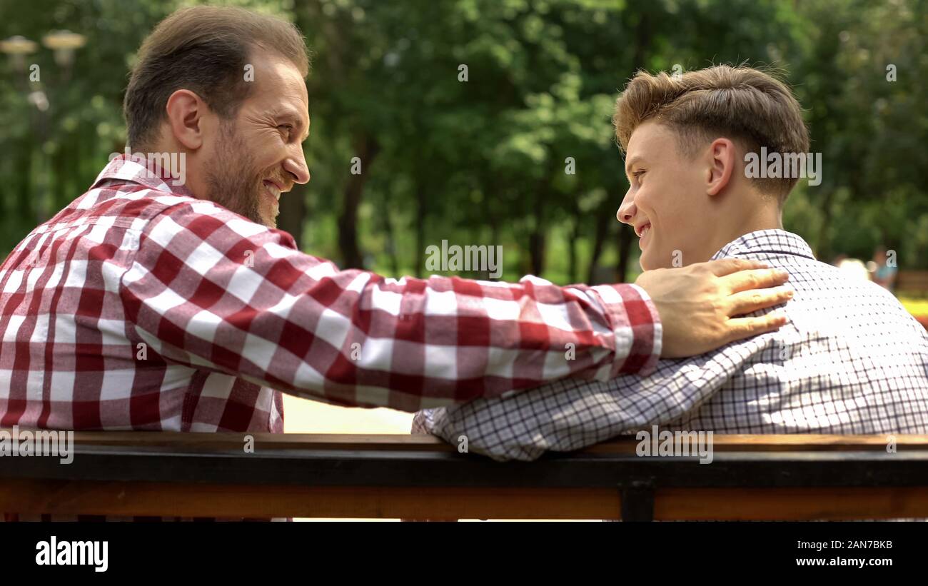 Teenage son talking with father on bench in park, dad supporting his ...